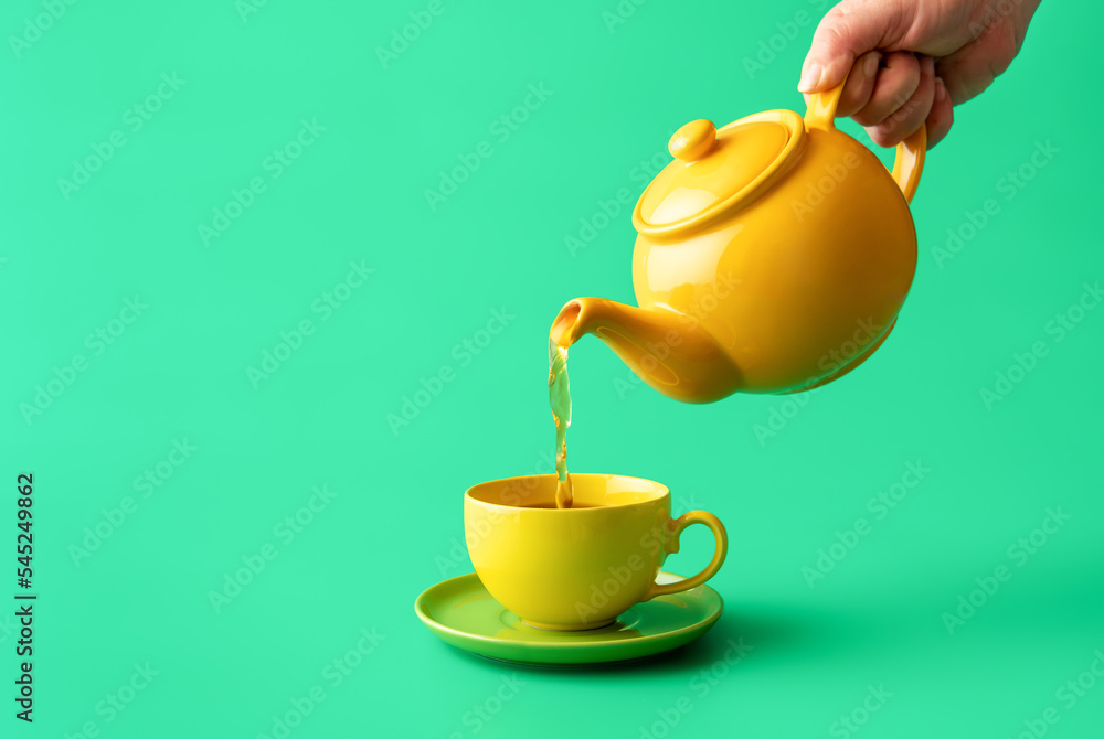 Pouring tea from a teapot in a cup, isolated on a green background ...