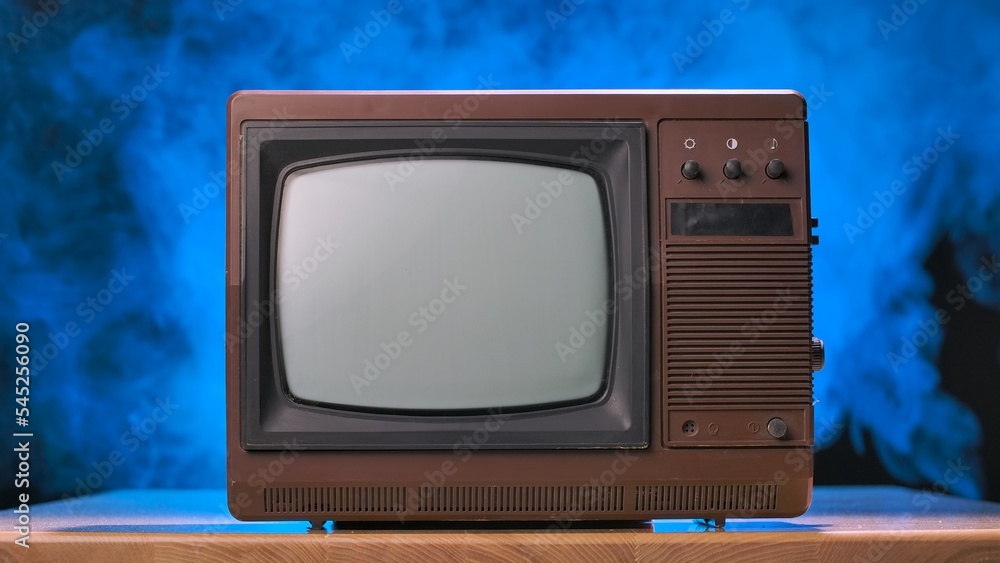 Old TV on a wooden table against black studio background with blue ...