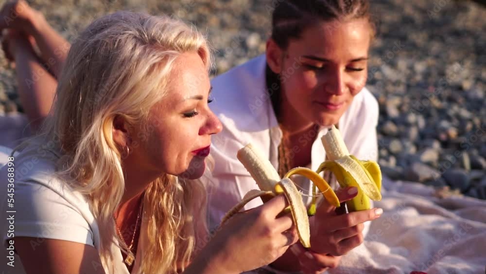 Two woman eating banana on the beach at sunset time. Girl Hand Holding ...