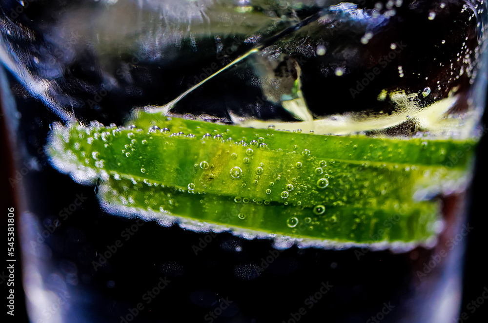 Gin tonic: Macro close up of green raw cucumber slices, sparkling bubbles and ice cubes in ...
