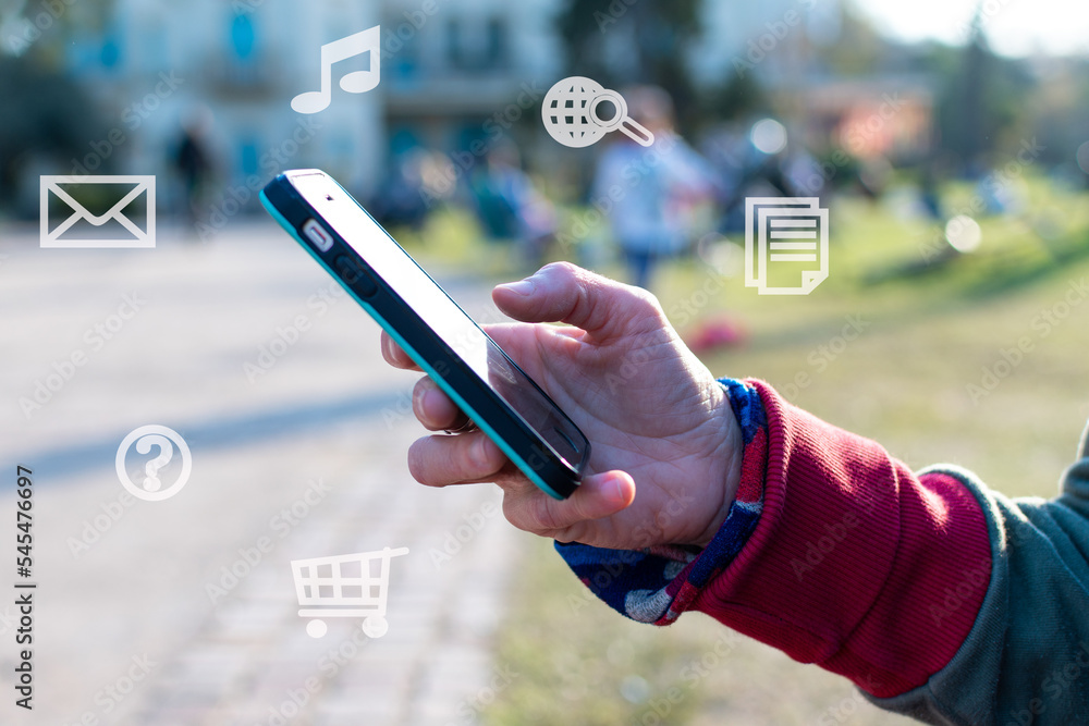 Hand with a smartphone outdoors and icons showing the variety of uses ...