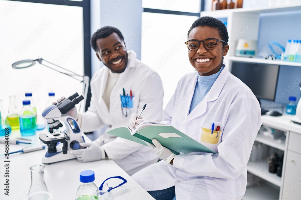 Man and woman scientists using microscope writing on notebook at ...