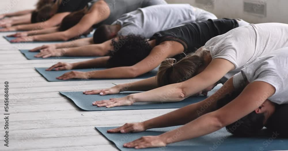 In row lying in Child Pose seven multi-ethnic people, yoga asana ...