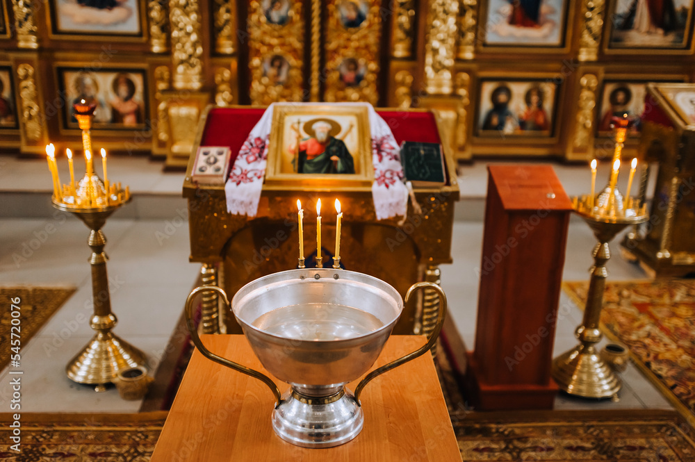 Burning candles in a candlestick, icons, a font, sacred water near the ...