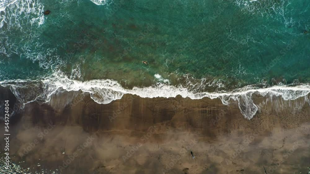 Ocean wave roll crash on shore in a straight line, sand dark volcanic ...