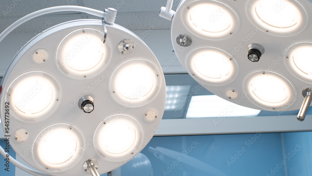 In the hospital, a surgical lamp shines under the ceiling above the ...