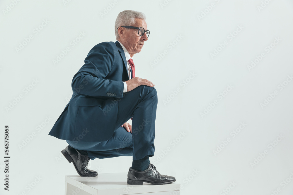 side view of crouched old man in his 60s wearing suit and looking to ...