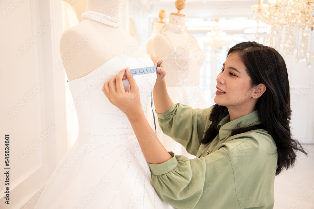 Owner of the wedding dress rental shop uses a tape measure to measure ...