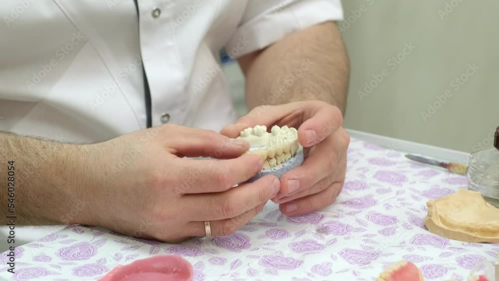 Dental technician looking at plaster cast of jaws while making denture ...