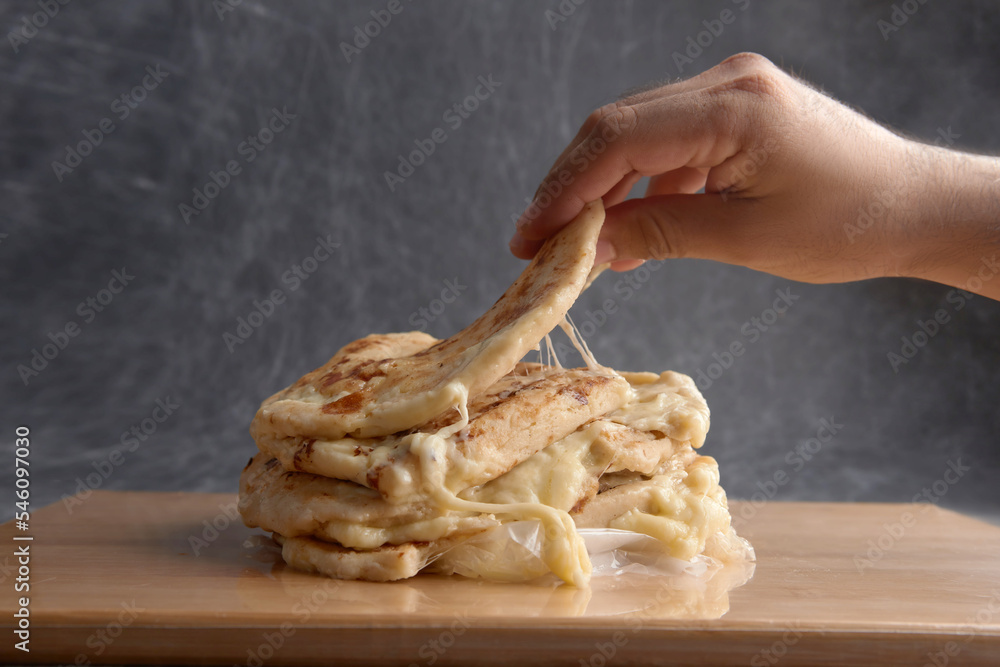 Hand picking a pupusa from a stack of pupusas on a wooden board and ...