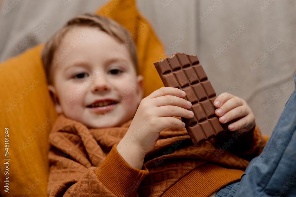 Little adorable boy sitting on the couch at home and eating chocolate ...