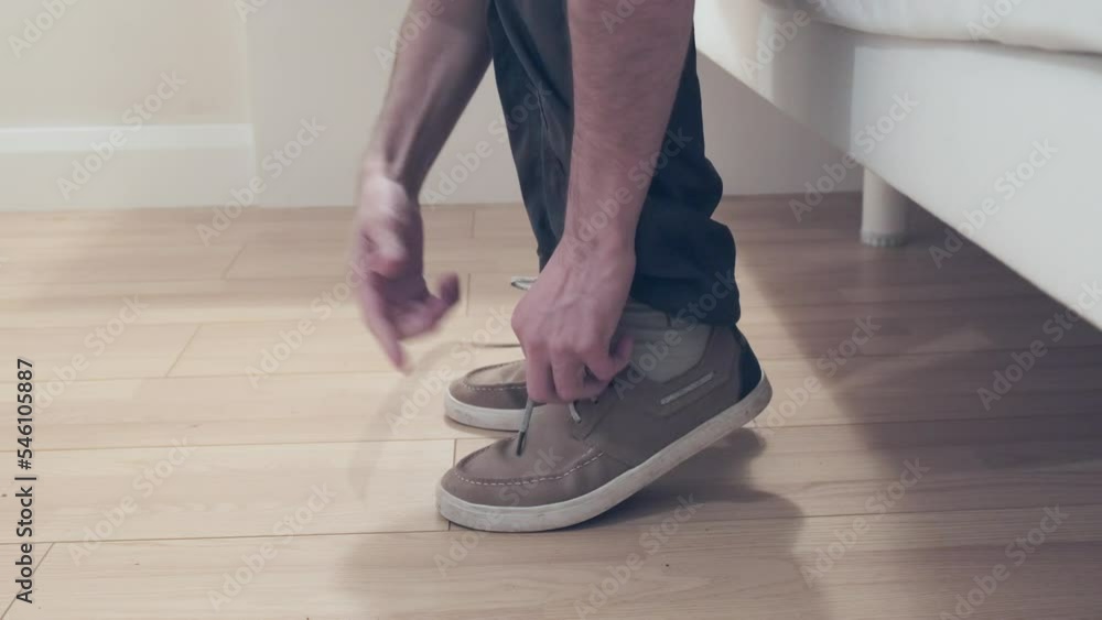 Man takes off his casual comfort shoes in front of bed. Lace untying ...