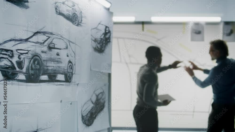 Two diverse automotive male engineers discussing sketch, drawing with ...