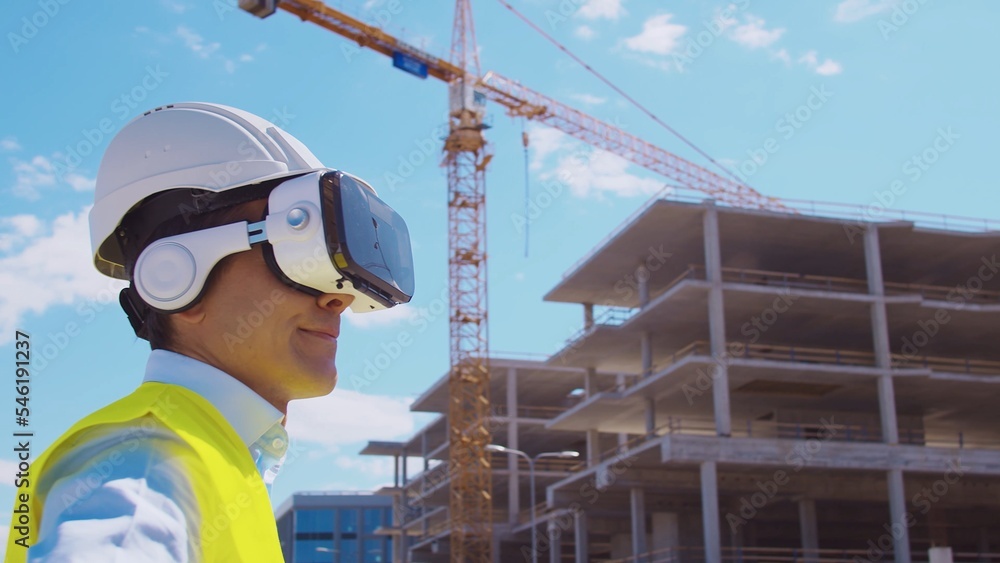 Professional builder in VR helmet standing in front of construction ...