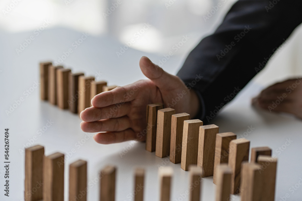 Businessman stops her hand blocking or falling dominoes Financial ...