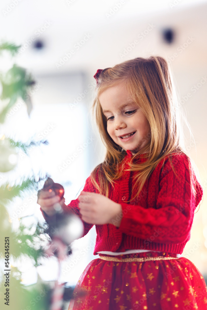 Portrait of a cute little girl decorating a Christmas tree at home for ...