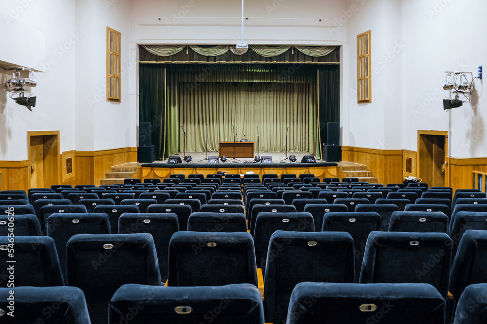 Assembly hall with stage for performance and rows of empty dark blue ...