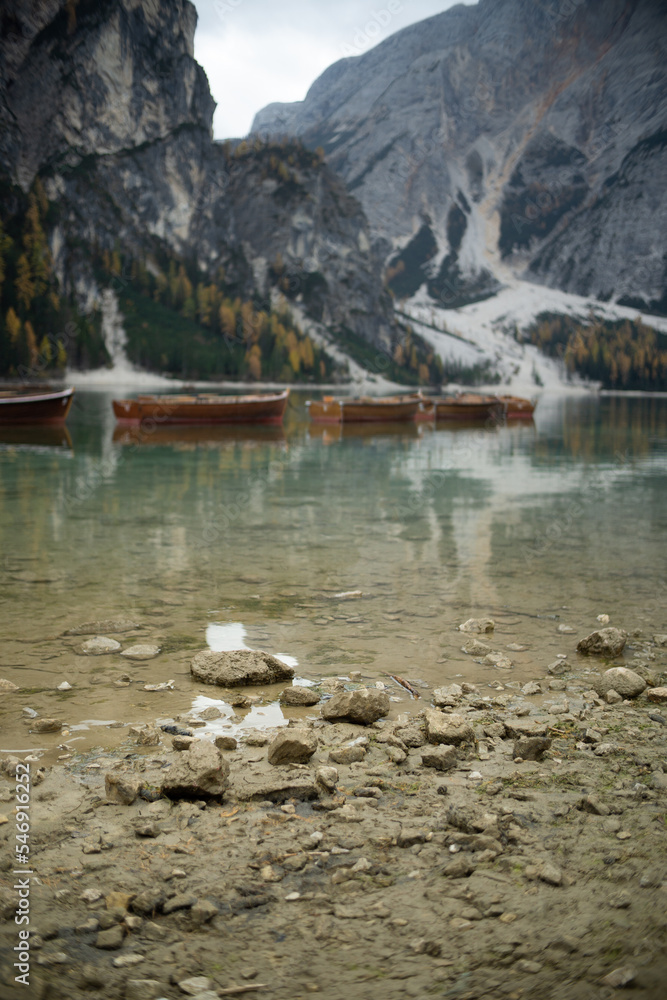 Primo piano di sassi sulla riva del lago, sullo sfondo barche in fila e ...
