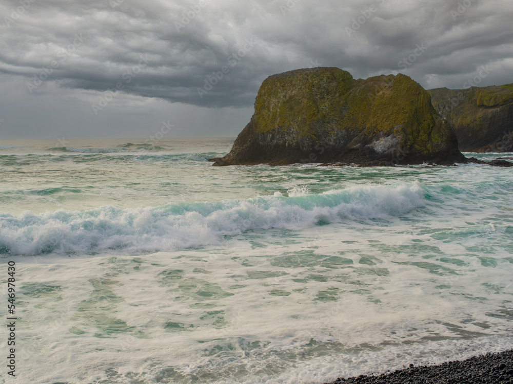 Raging ocean, white foamy waves breaking on the shore. In the distance ...