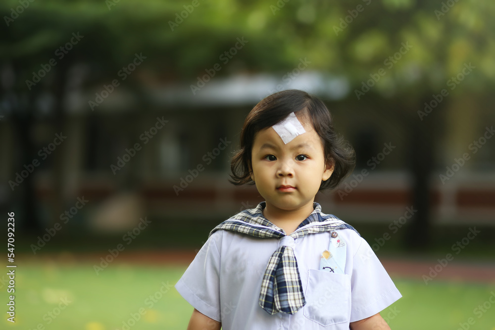 An Asian little girl who wearing a kindergarten uniform and has a wound ...