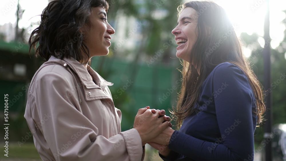 Happy female friends laughing and smiling standing outside in sunlight ...
