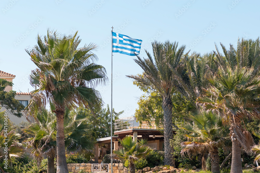 Greek flag waving in the wind surrounded by palm trees and beach ...