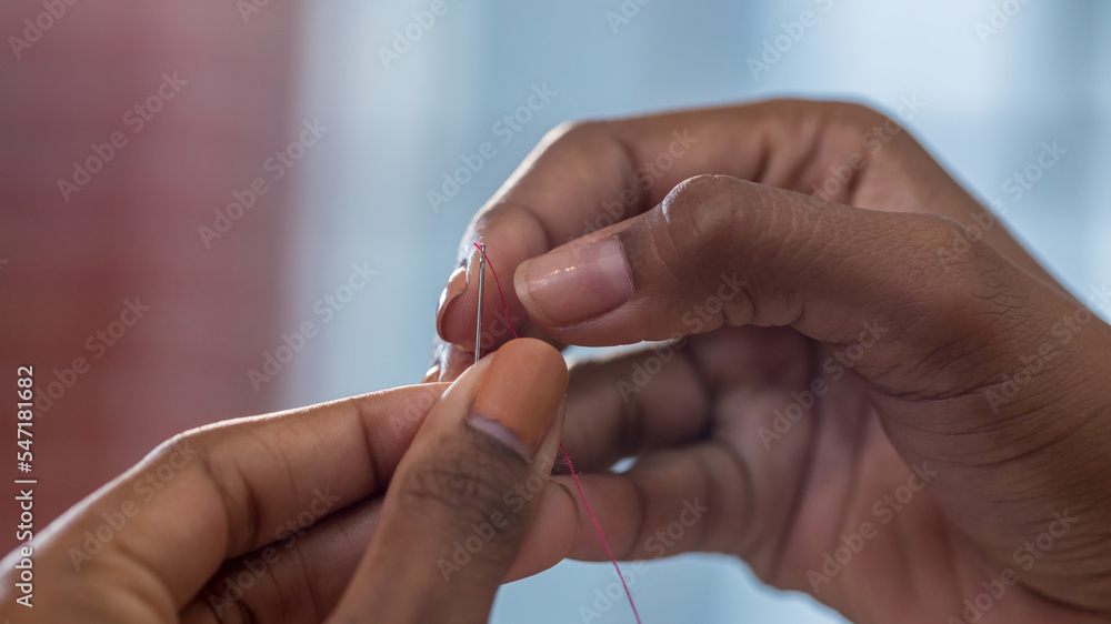 Thread into the needle. Hands of woman pulling thread into the needle ...