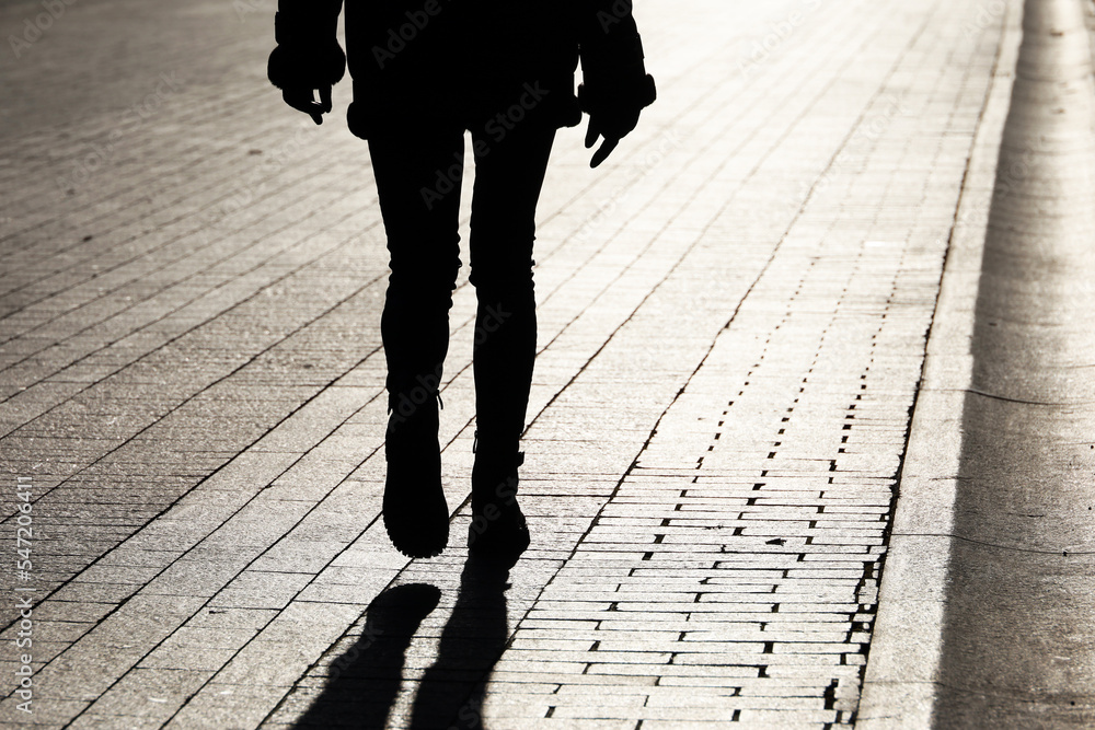 Black silhouette and shadow of lonely slim girl walking on a street ...