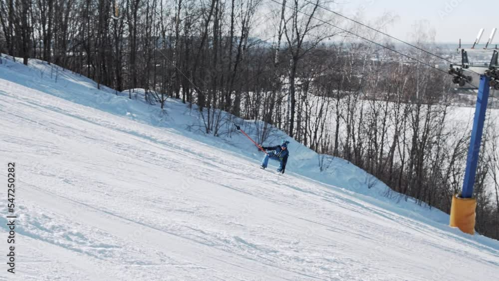 A snowboarder climbs up on a hill using a T-bar lift on a sunny day at ...