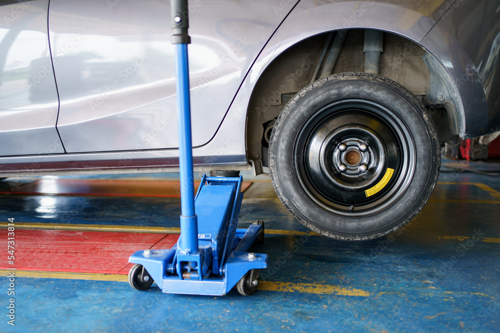 Technician or repairman using a hydraulic jack lift up a car at rear ...