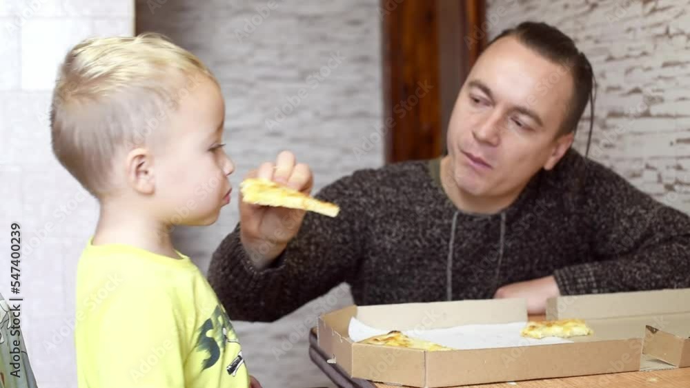 Caucasian kid boy and his father eating pizza. Father feeds his son ...