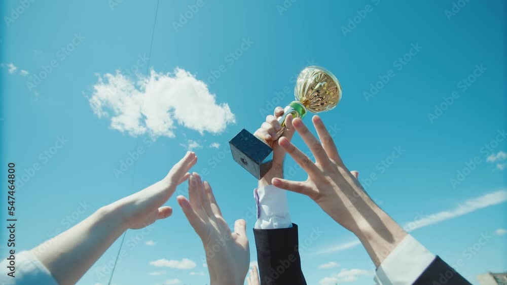 One hand with a white sleeve holds golden cup trophy high in the air ...