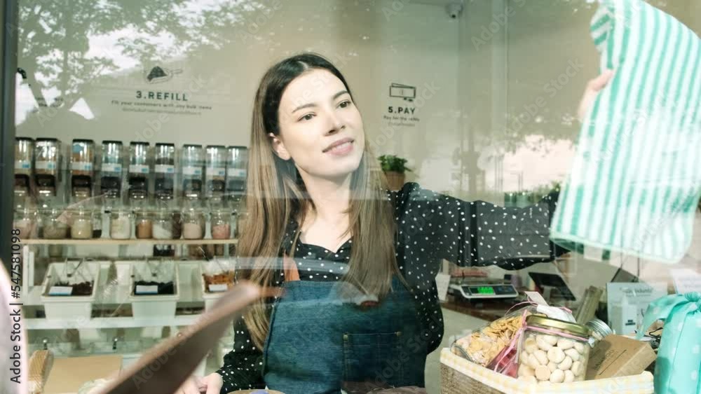 Young Caucasian female shopkeeper works by cleaning glass window ...