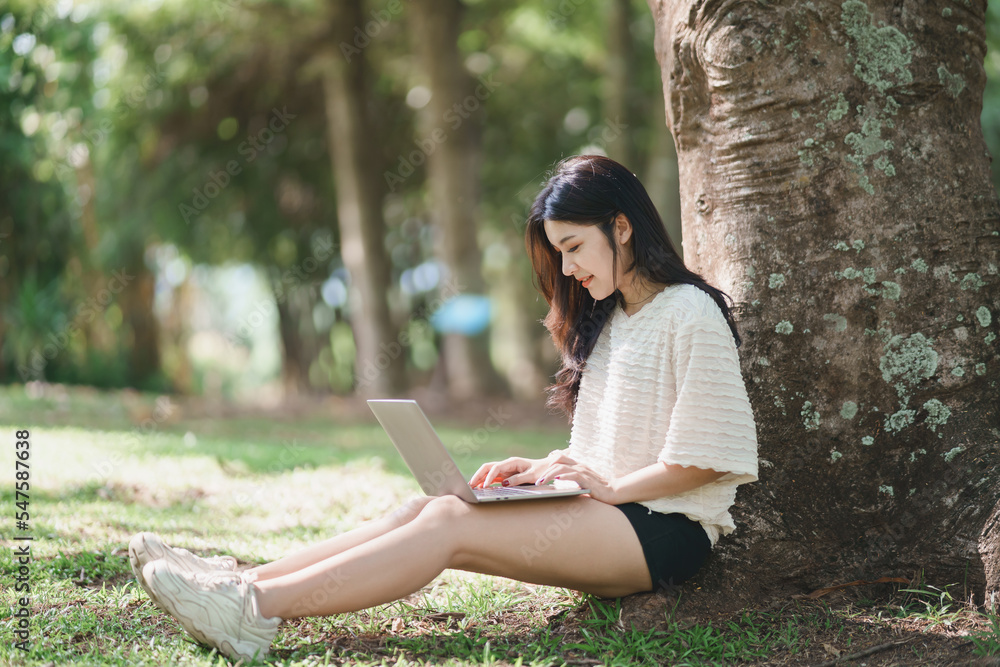 Asian woman sitting on picnic and lawn at park working on laptop. Asian ...