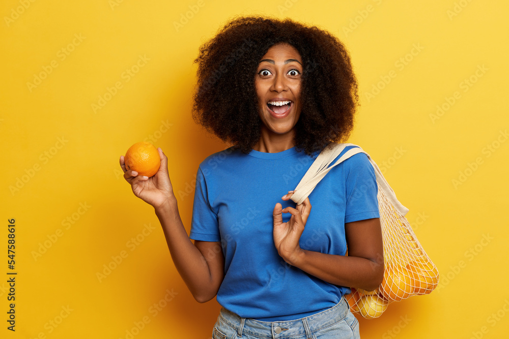 Dark skinned curly haired young woman holds an orange with happy face ...