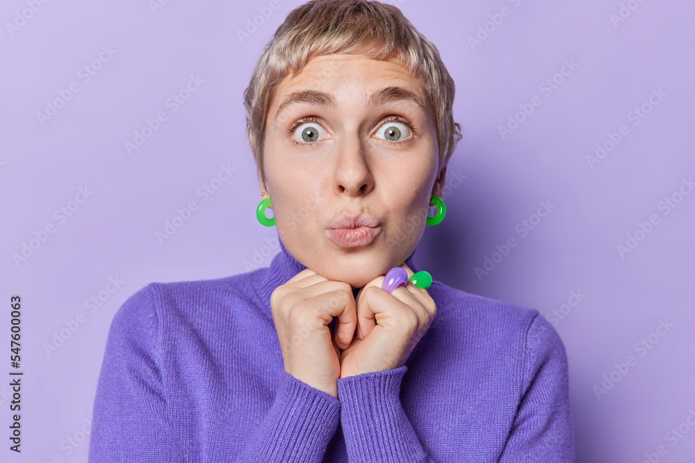 Portrait of shocked short haired female model keeps lips rounded hands ...