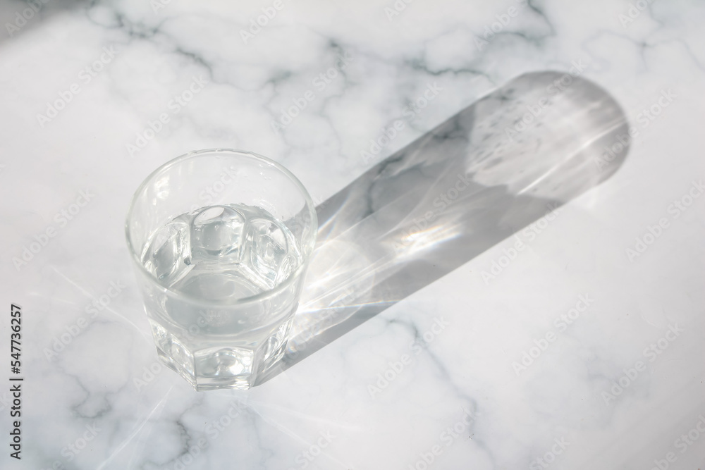 glass with sparkling sunlight shadow on the white background. Minimal ...