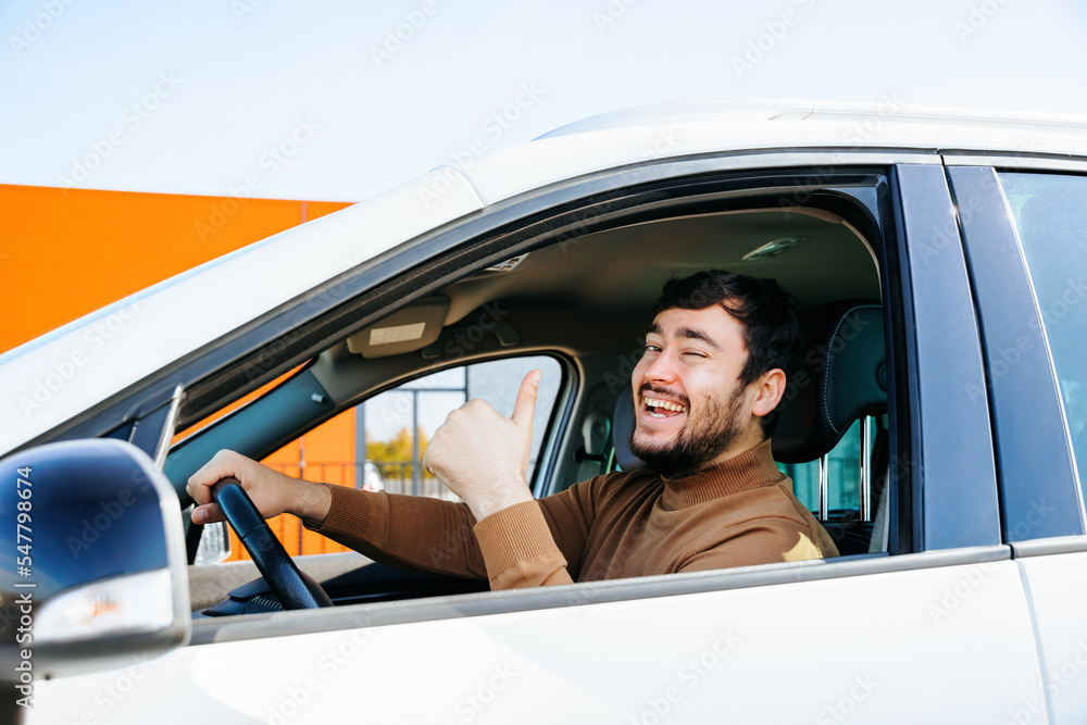 modern satisfied chauffeur bearded young man sitting in a car shows ...