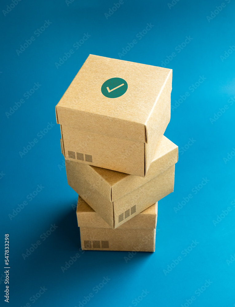 Green check mark icon on lid of cardboard parcel boxes stack on blue ...