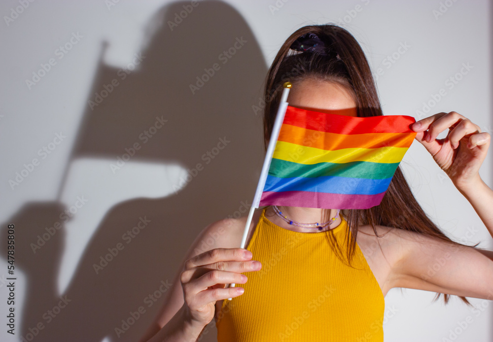 Young faceless gay woman, girl hides face behind rainbow LGBT flag ...