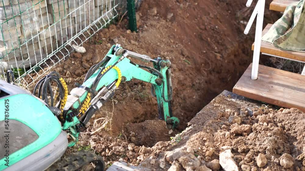 Mini excavator digs a trench to lay pipes. Close up of an excavator ...