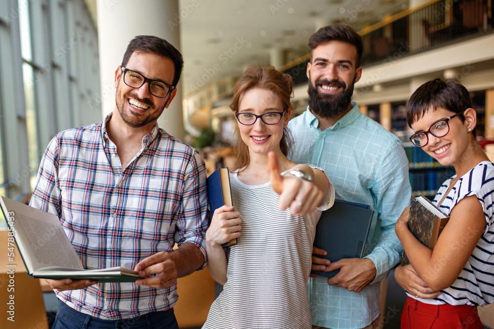 Happy university students studying with books in library. Group of ...