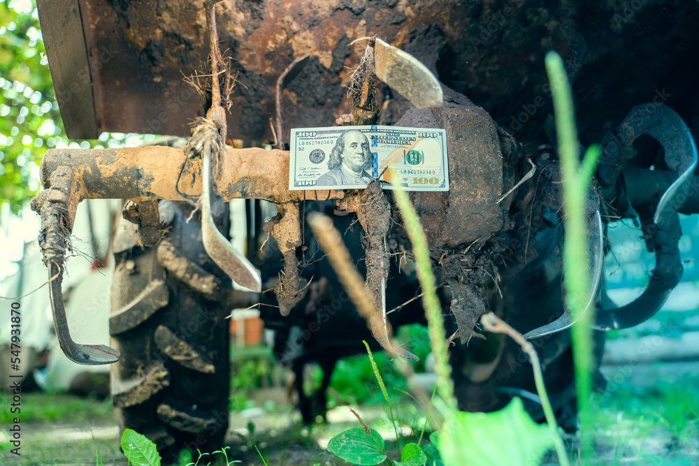 One hundred us dollars on a mini tractor rototiller close-up. Money and ...