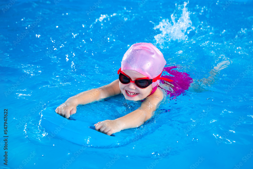 Smiling little girl learning to swim in indoor pool with flutterboard ...