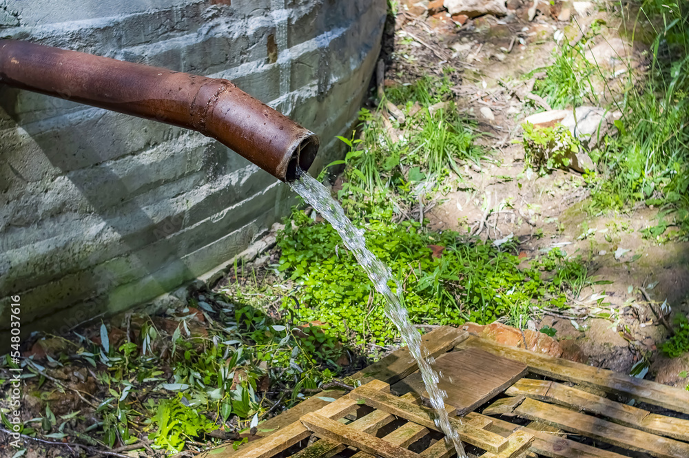 Pure spring water flows from the pipe. Summer, against the backdrop of ...