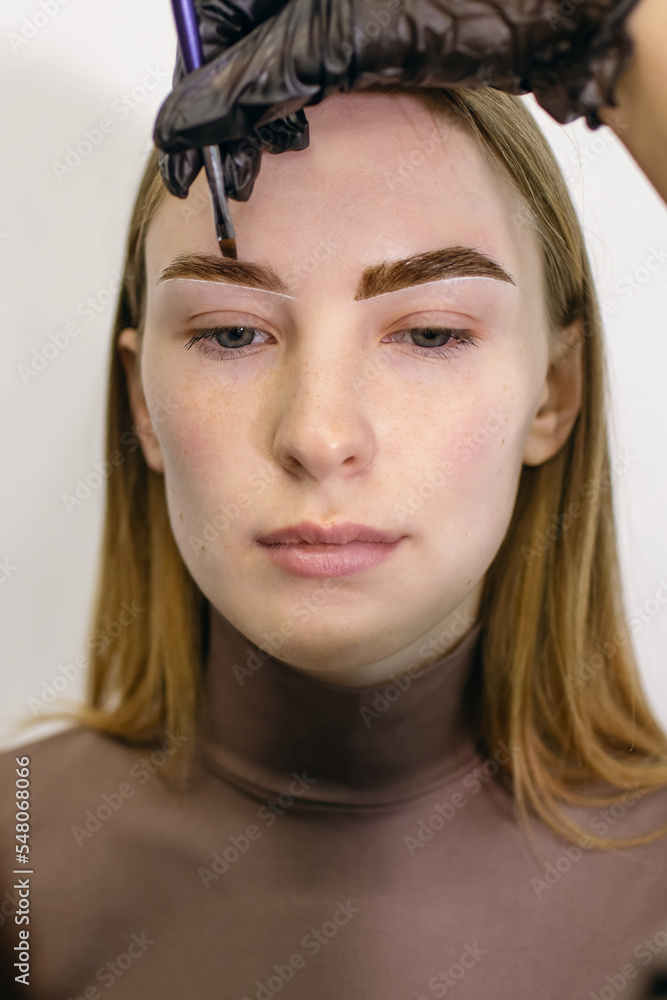 Eyebrow master shapes and paints with a brush the eyebrows of a red ...