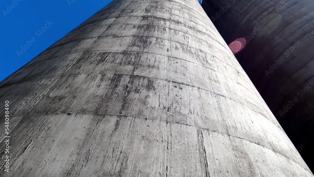 Close-up along surface of large concrete silo under clear blue sky and ...