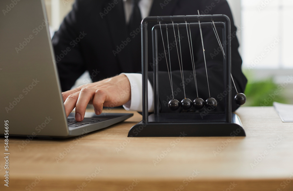 Businessman working on laptop computer at his desk with Newton's cradle ...
