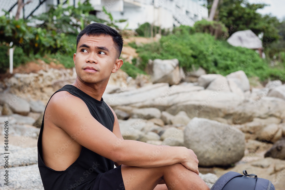 Filipino man sitting on rocks looking up to the side. Pensive male ...