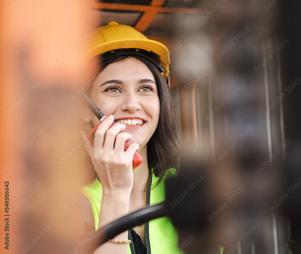 Female foreman using radio while driving forklift vehicle at shipping ...